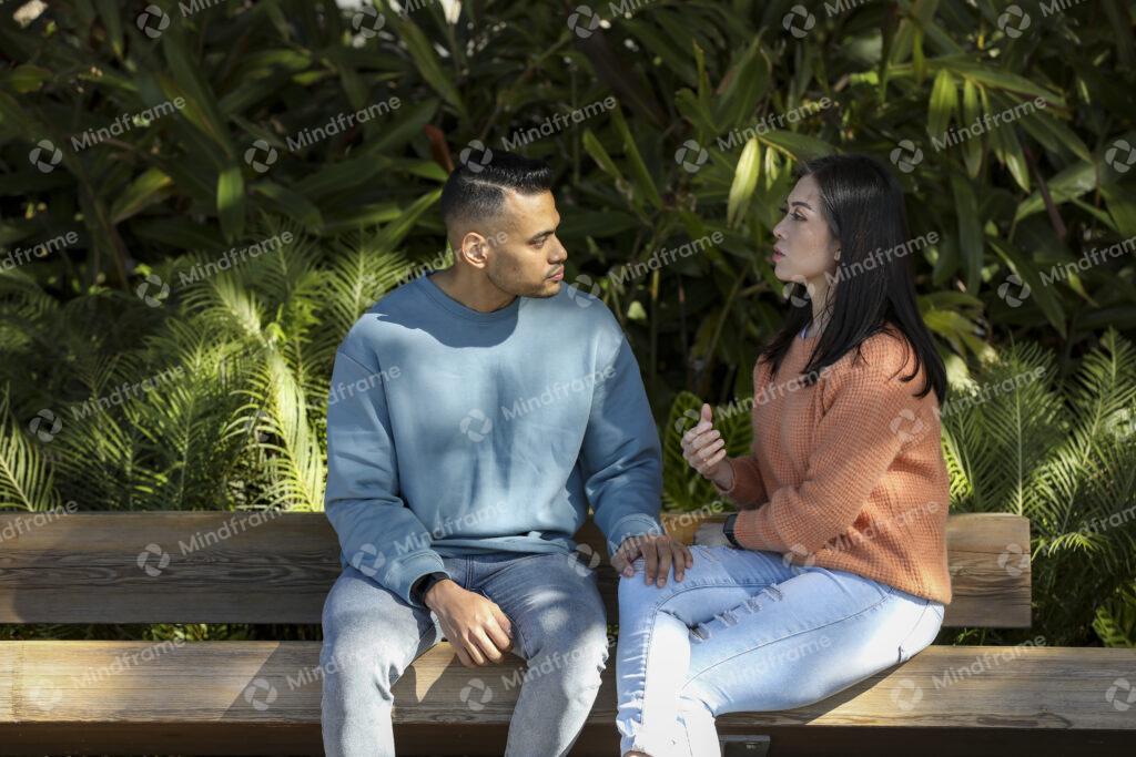 Two people sitting on a park bench and talking to each other ...