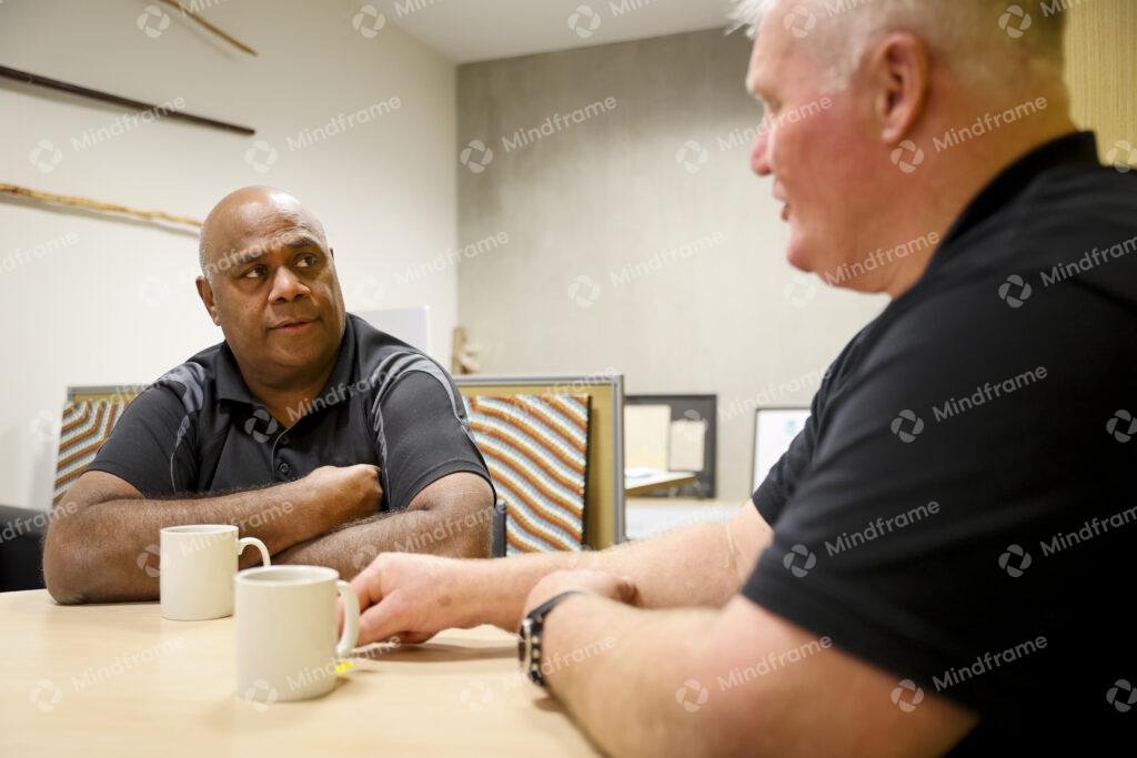 Two men sitting at a table indoors having a conversation – Mindframe ...